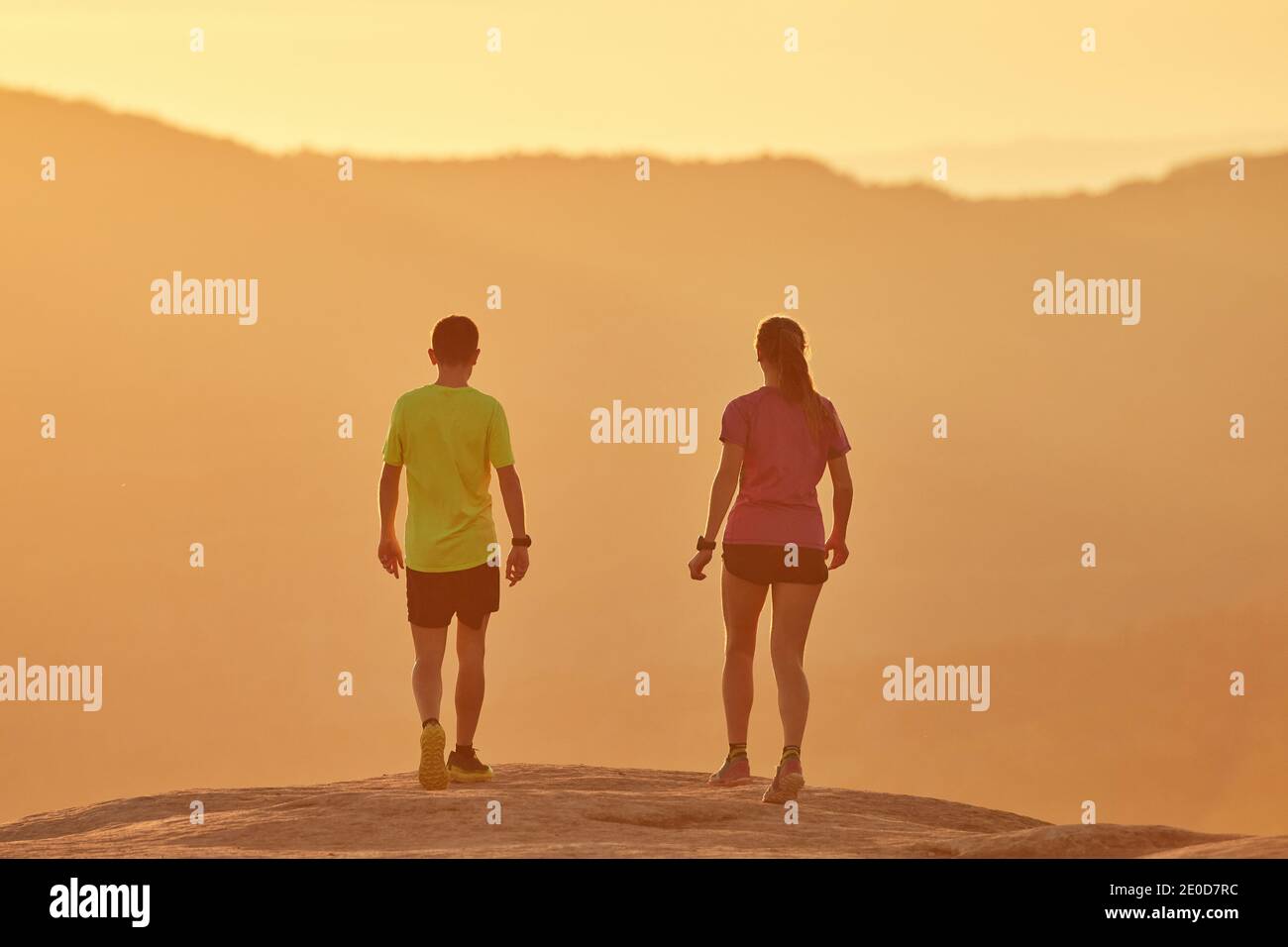 Back view of male and female runners walking on hilltop in mountains at ...
