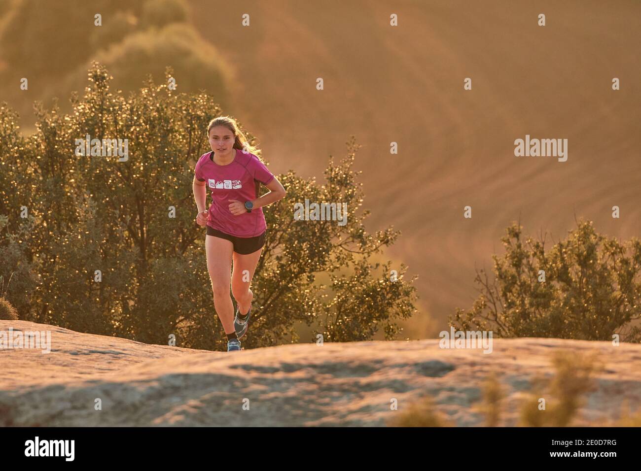 Female athlete running up rocky hill at sunset in mountains during ...