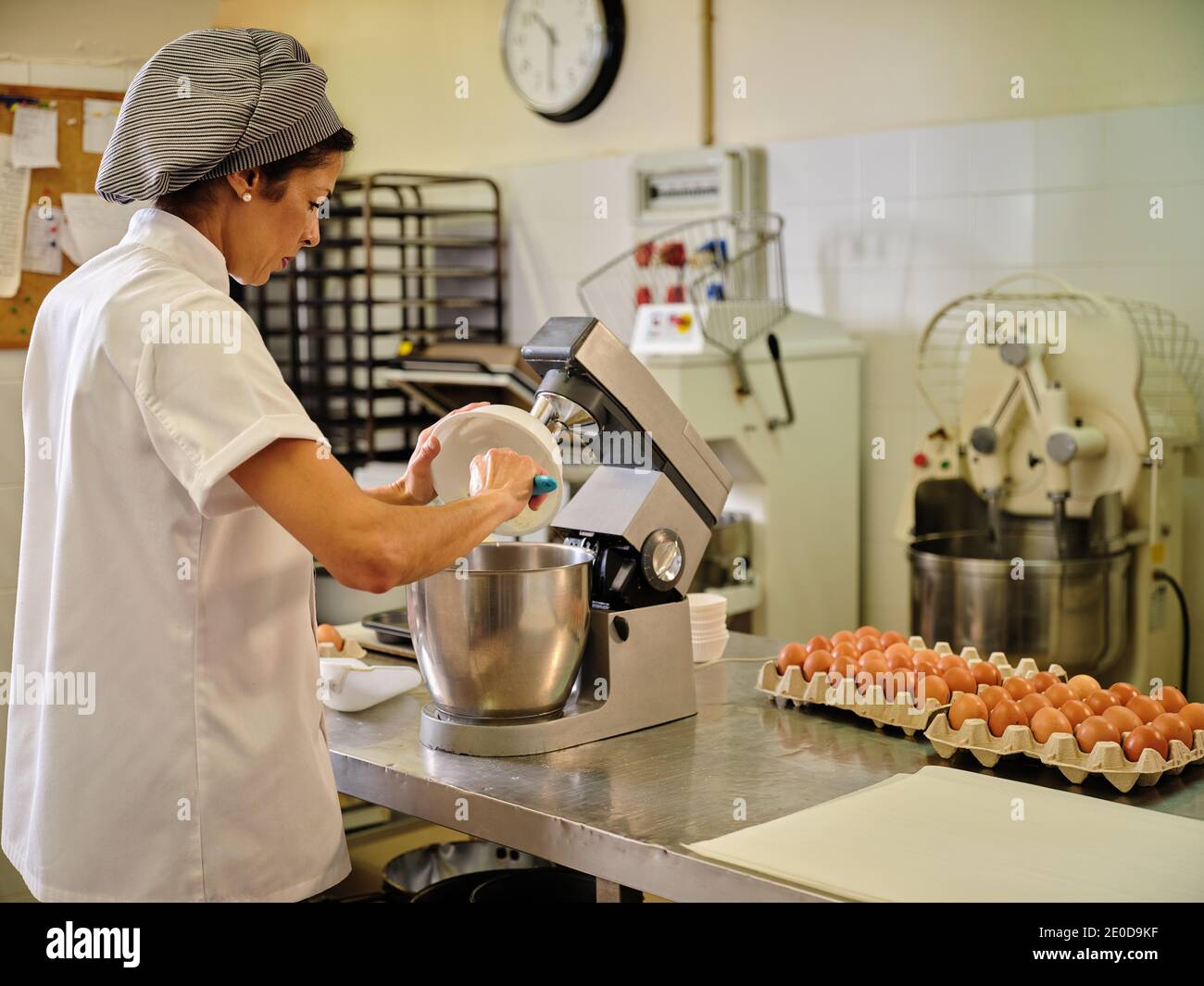 Side view of female baker with spatula and mixer attachment in hands ...