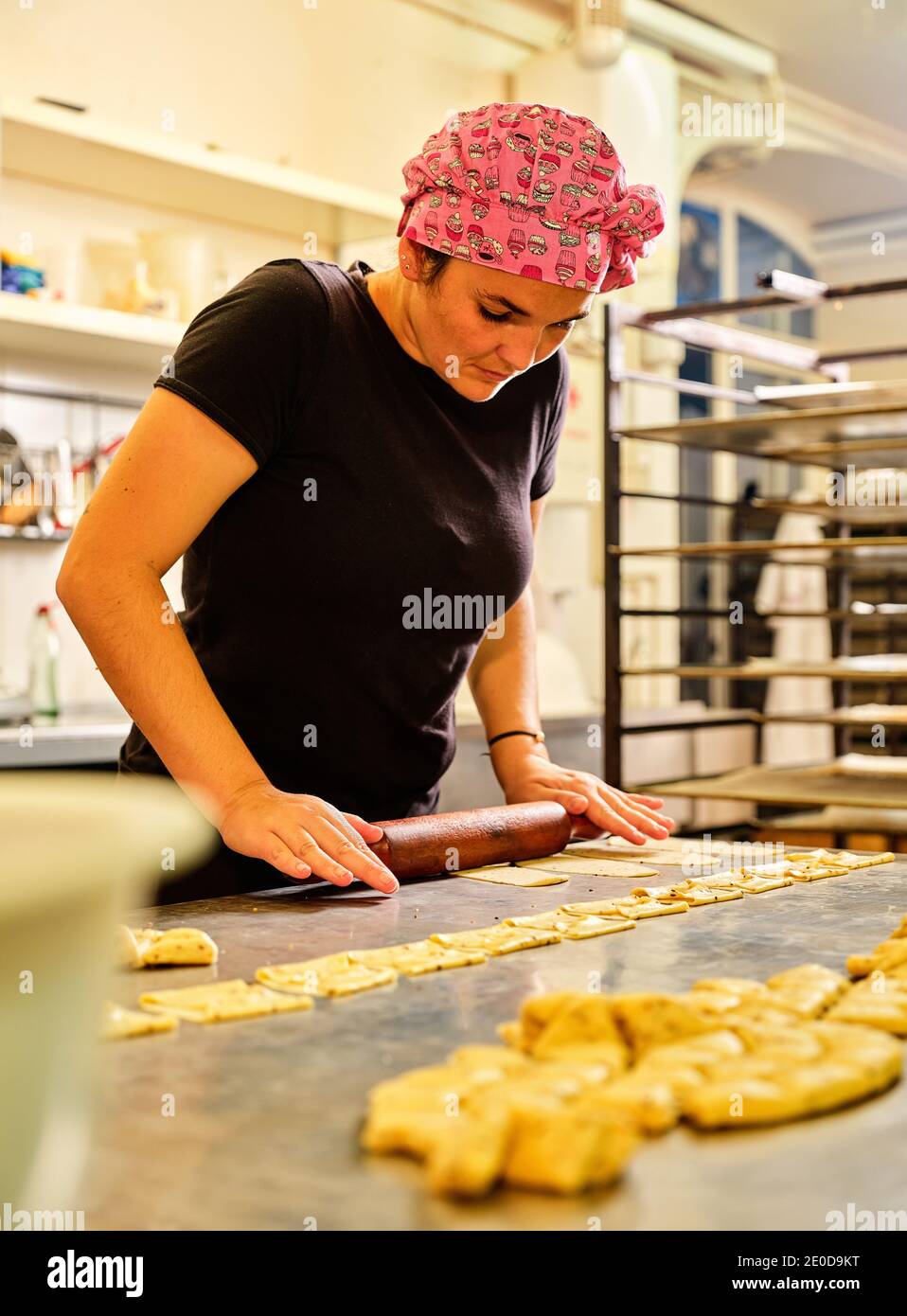 Concentrated skilled female pastry chef rolling small pieces of dough ...