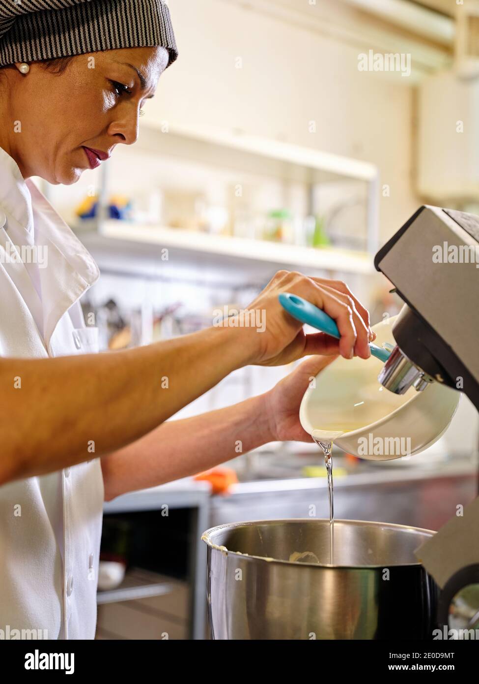 Side view of female baker with spatula and mixer attachment in hands ...