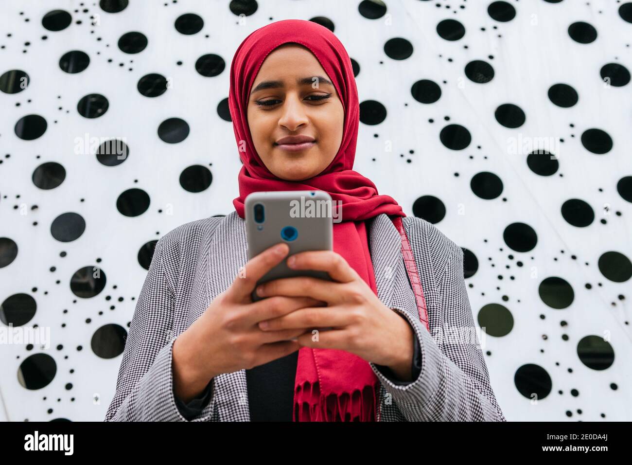 Side view of cheerful Arab female in hijab standing sending message on ...