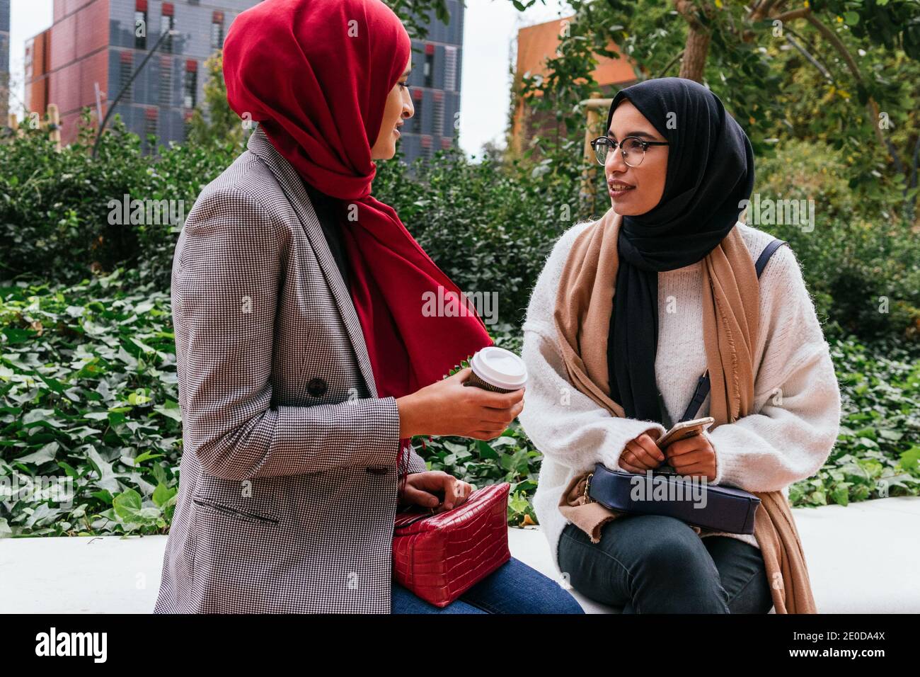 Friendly Arab female friends sitting on street and talking to each ...