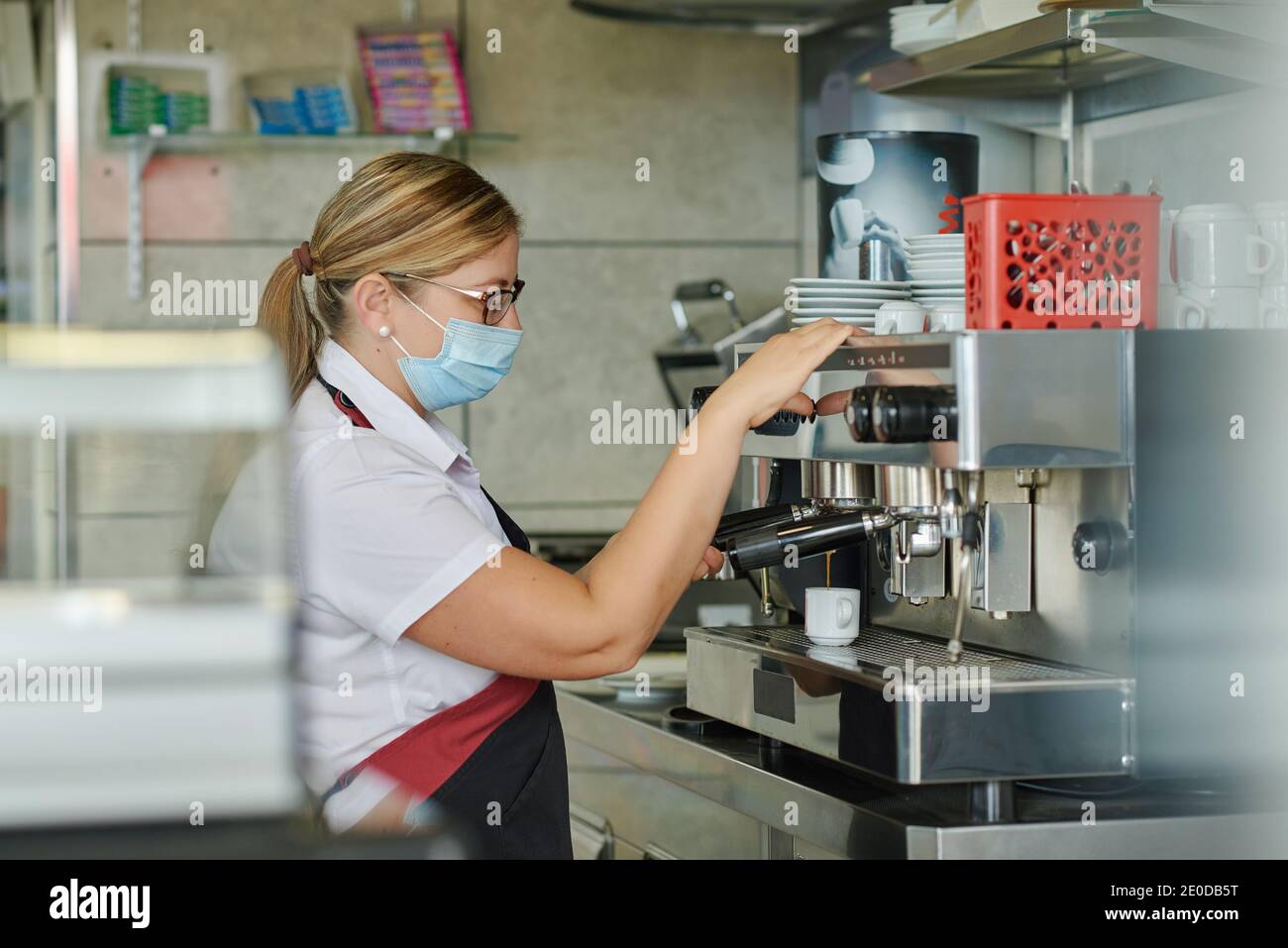 Side view of female barista in medical mask using coffee machine and ...