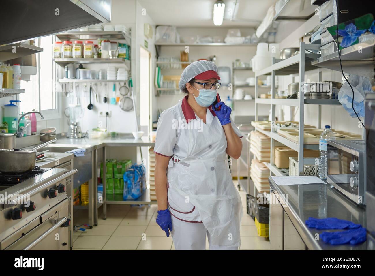 Female cook in white uniform and protective mask and gloves speaking on ...