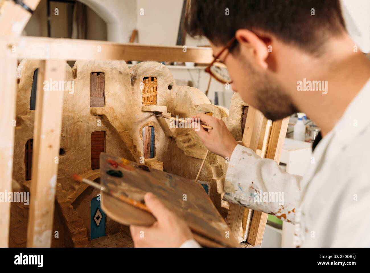 Side view of talented male artisan in dirty robe painting handmade ...