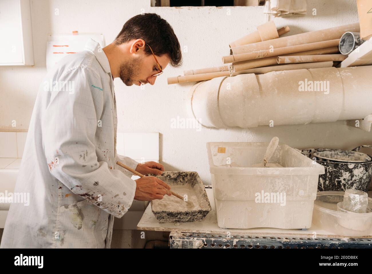 Side view of serious male artisan pouring liquid gypsum in wooden form ...