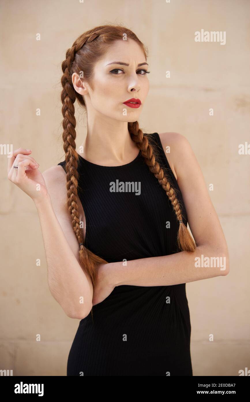 Stylish female model with red hair and braids sitting in studio on dark ...