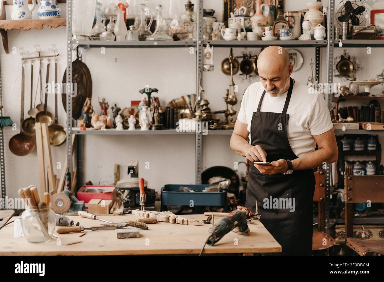 Serious middle aged male carpenter in apron messaging on mobile phone ...