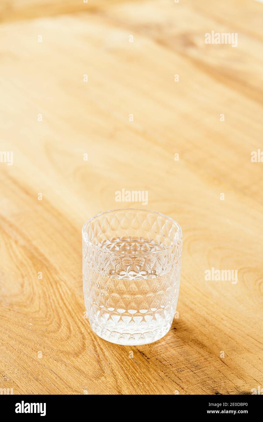 High angle of faceted glass with fresh water placed on wooden table ...