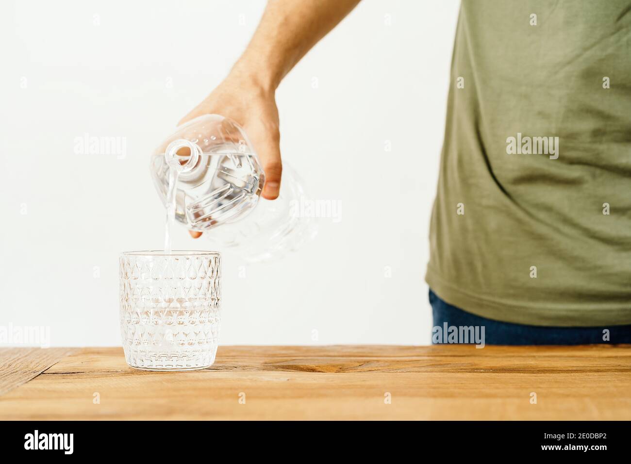 Crop anonymous male filling glass with fresh mineral water from plastic ...