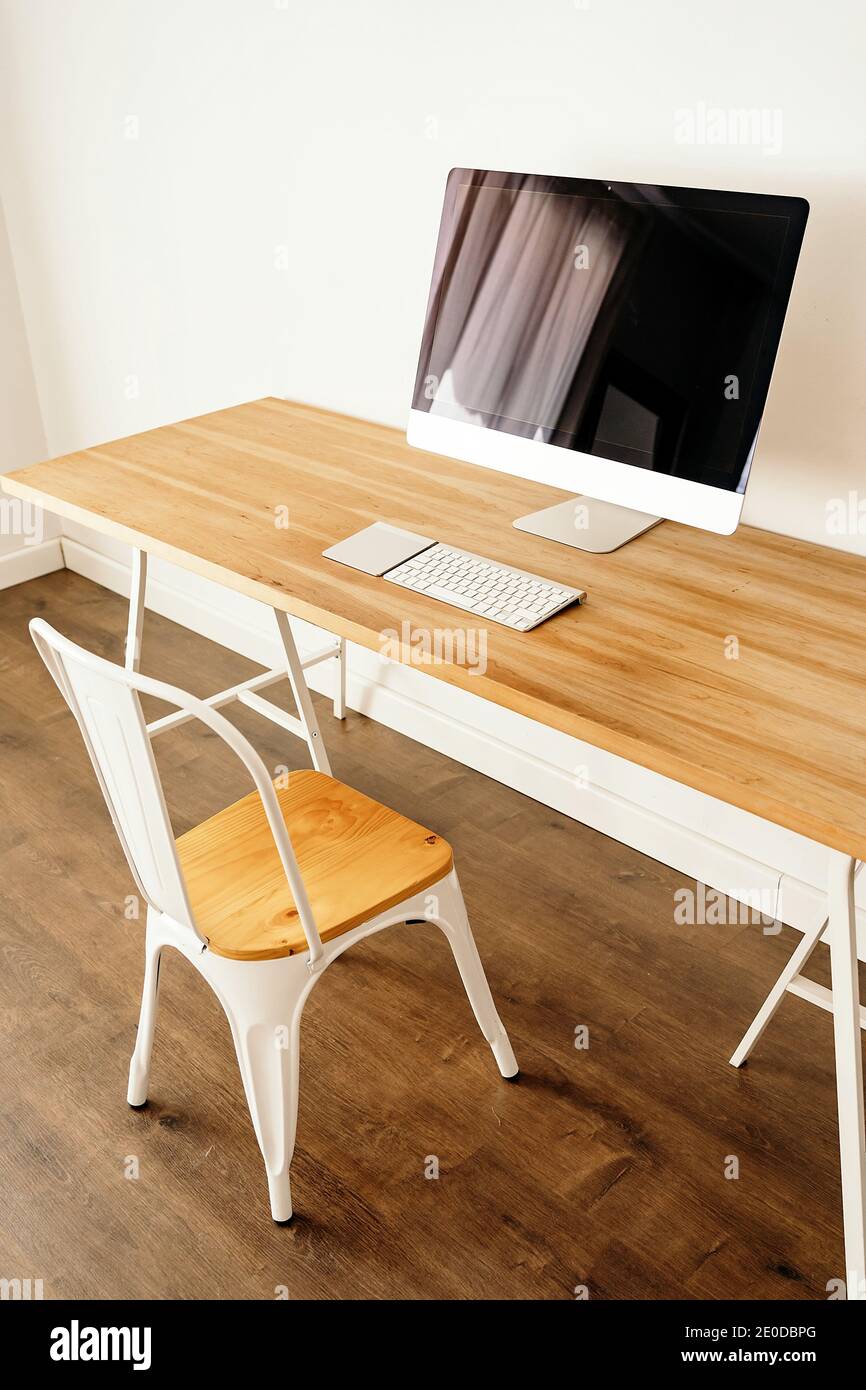 Modern computer placed on wooden table near chair in contemporary light ...