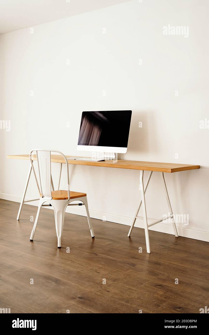 Modern computer placed on wooden table near chair in contemporary light ...