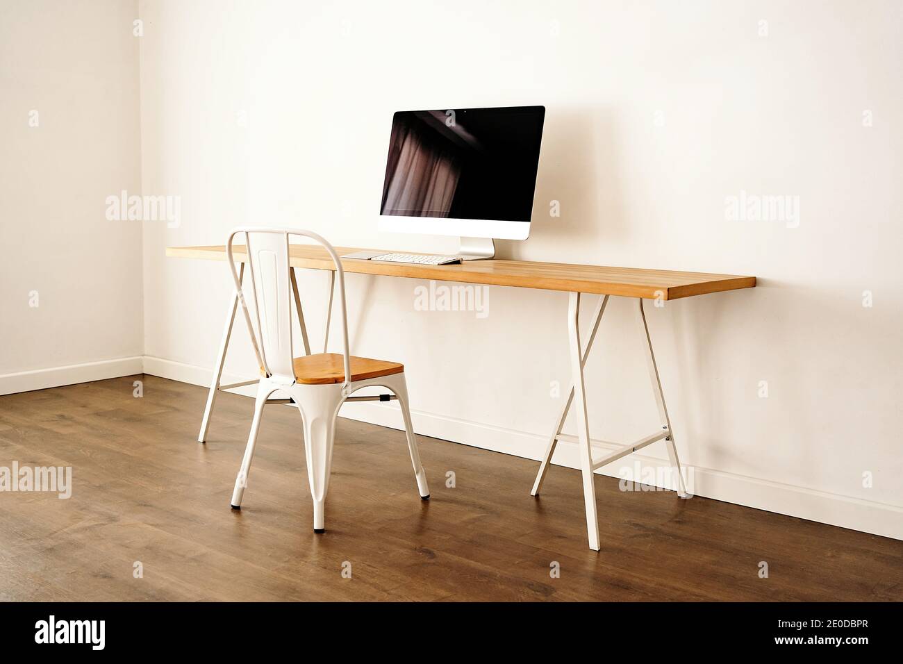 Modern computer placed on wooden table near chair in contemporary light ...