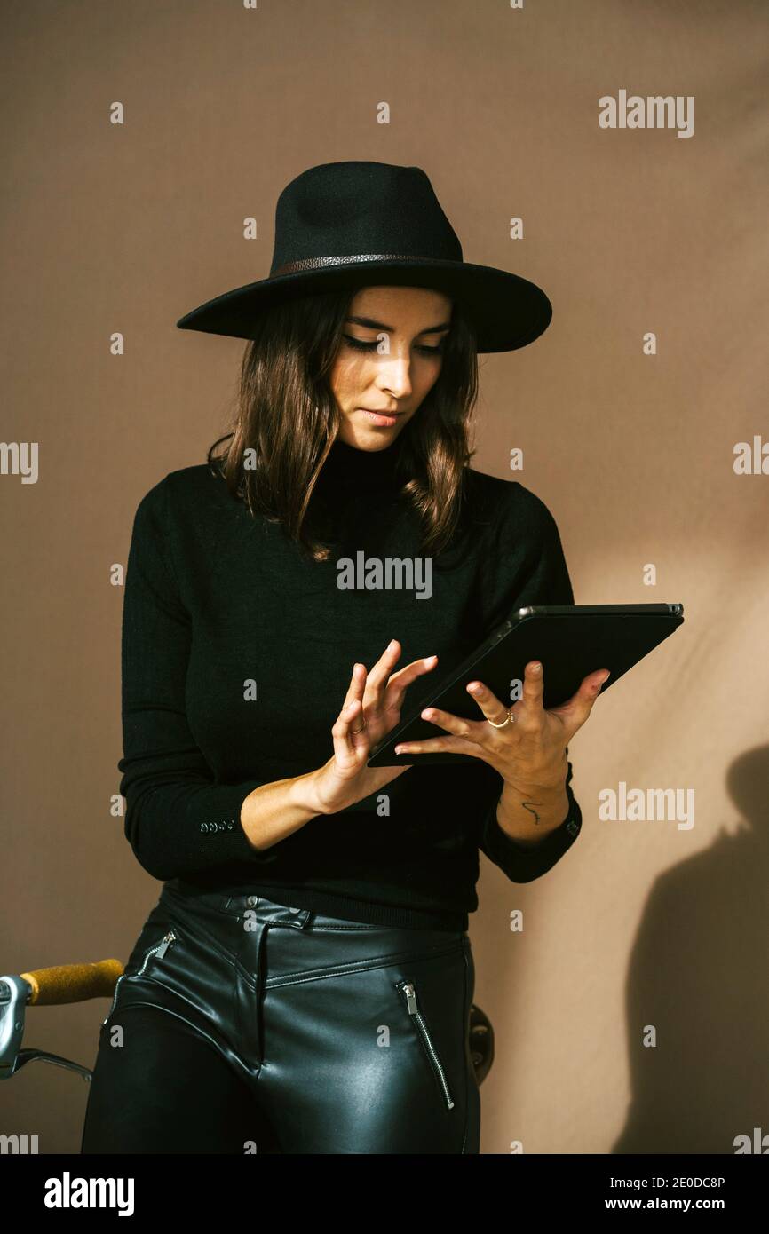 Young female in trendy black leather pants and hat checking information ...