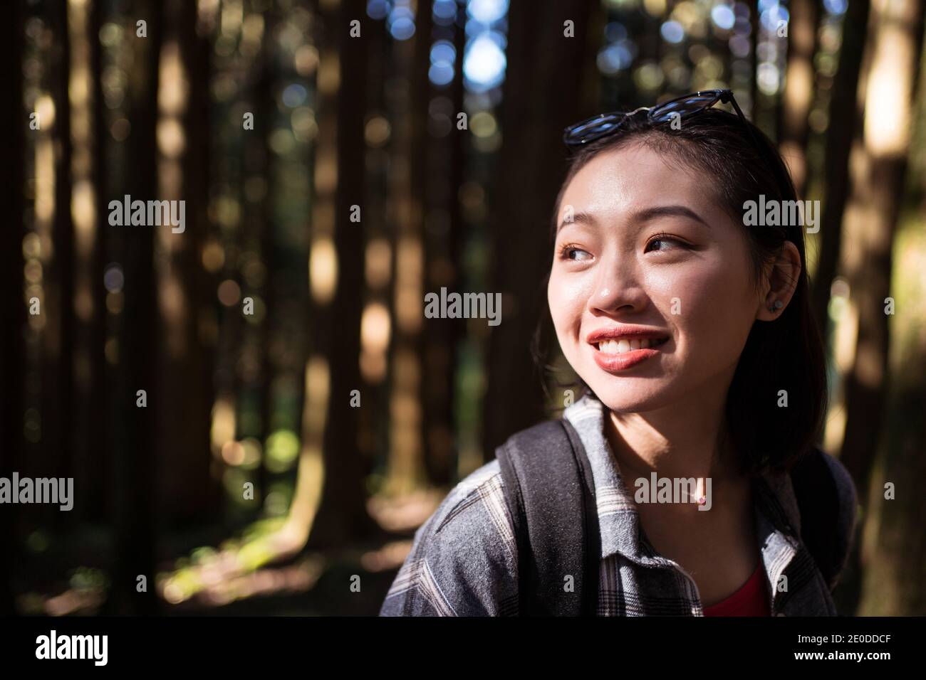 Smiling Asian female explorer with backpack standing in woods and ...