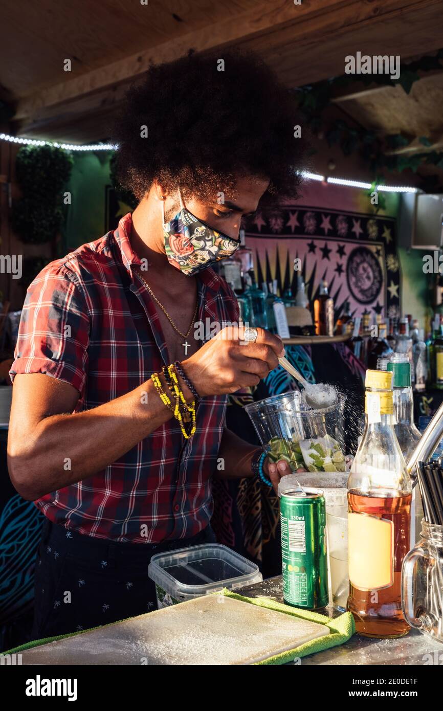 African American male barkeeper in protective mask garnishing cocktail ...