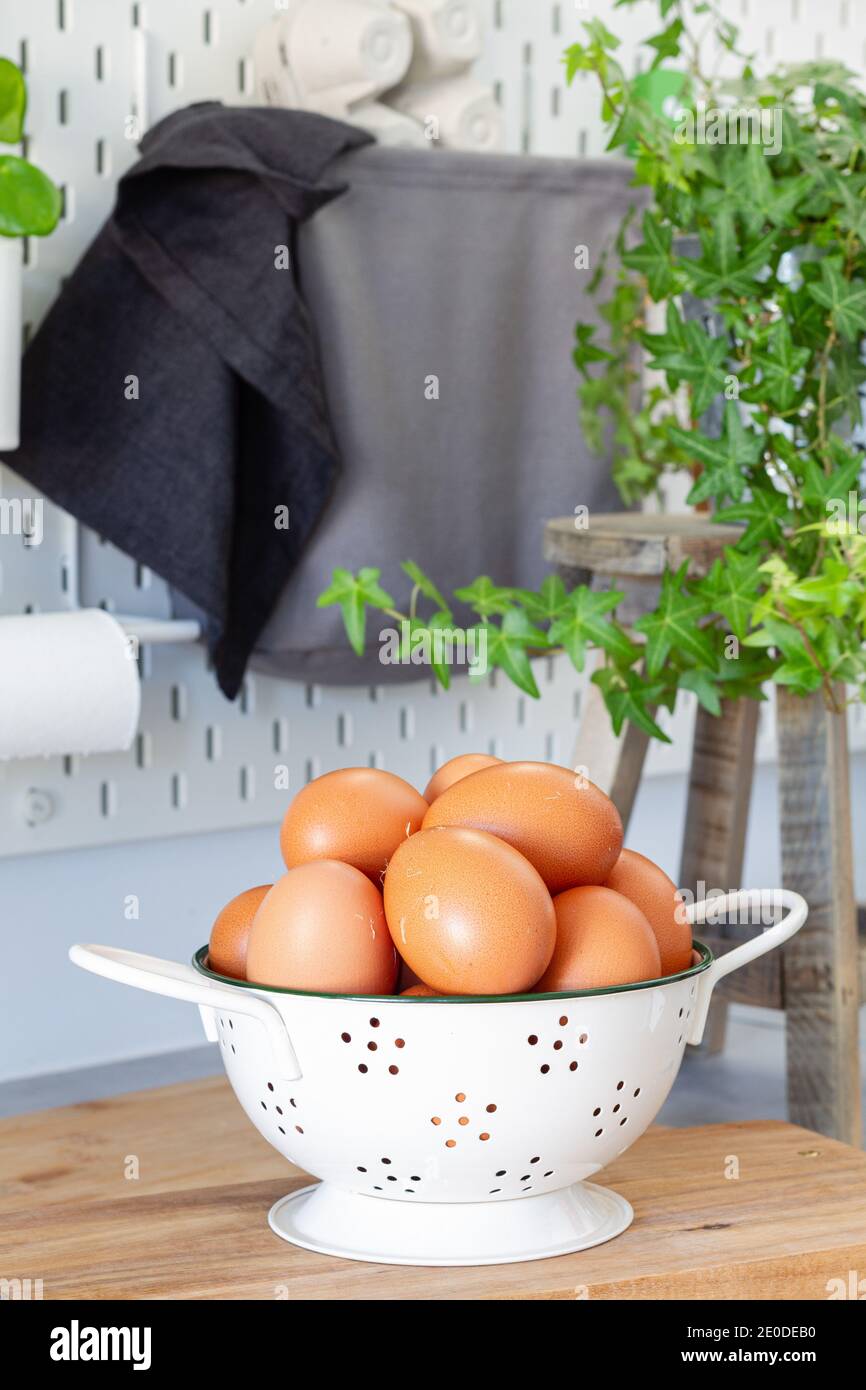 Heap of brown chicken eggs in white colander placed on table in cozy ...