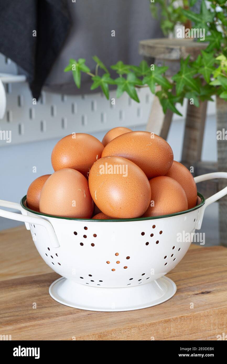 Heap of brown chicken eggs in white colander placed on table in cozy ...