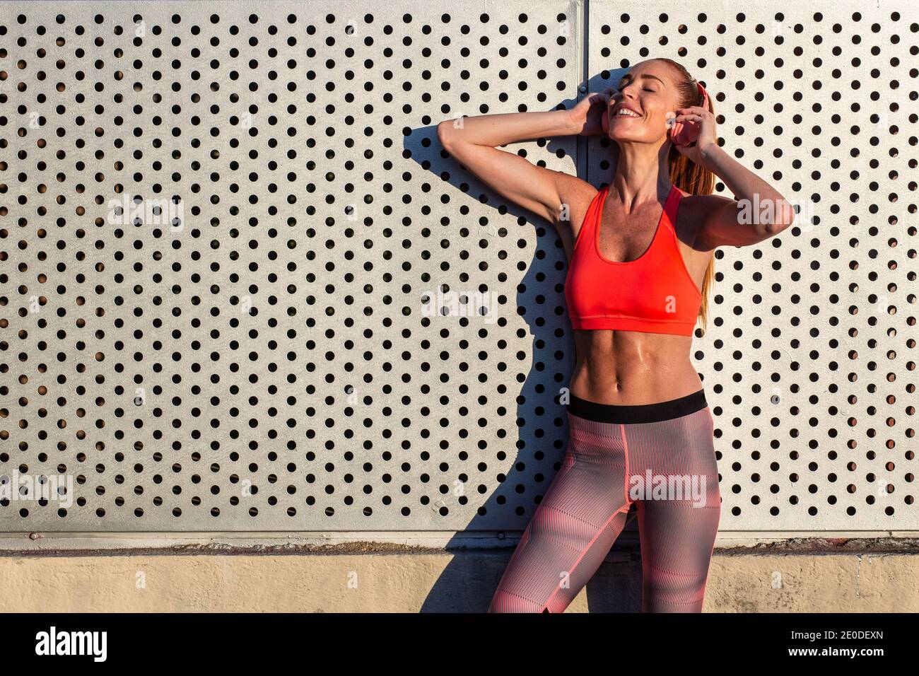 Carefree female runner in sports bra and leggings standing on street ...