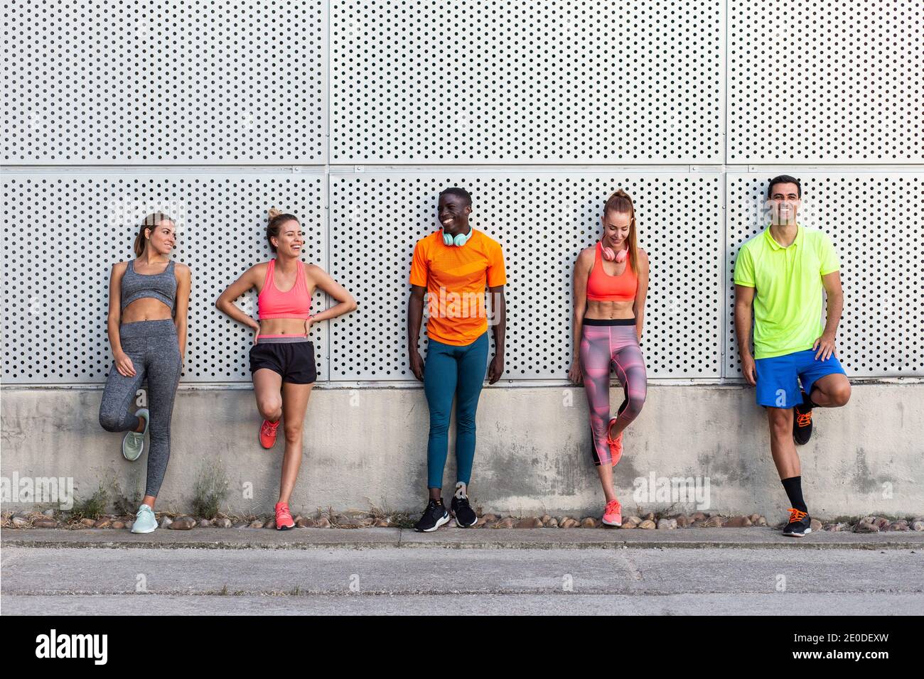 Group of cheerful multiethnic fit runners in sportswear leaning on wall ...