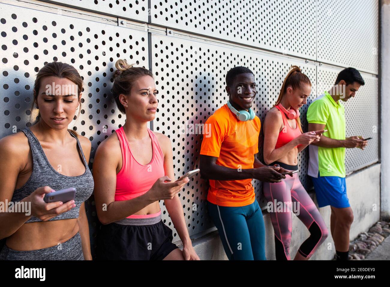 Group of multiracial runners in activewear leaning on wall of building ...