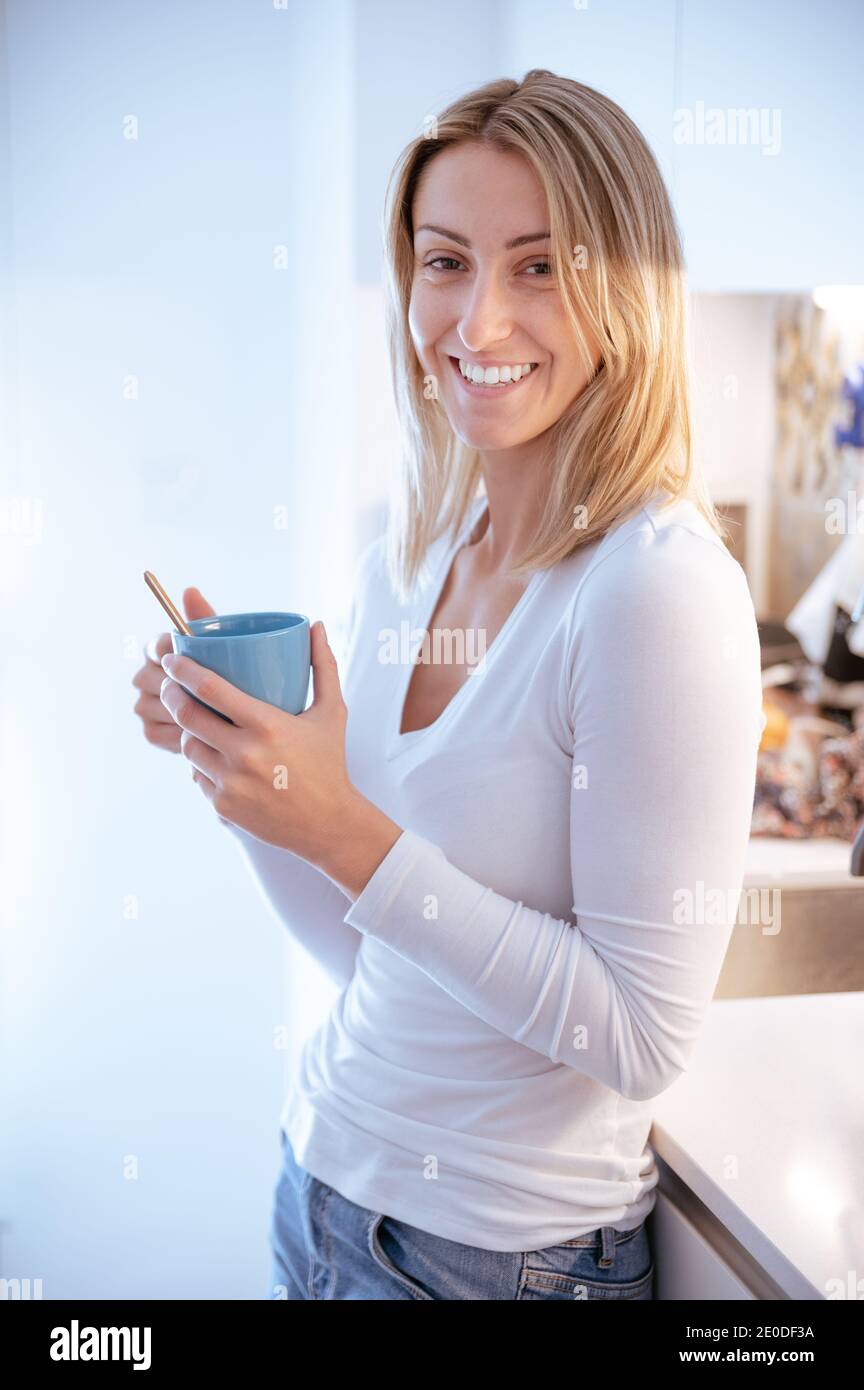 Young fit female in casual outfit standing in modern kitchen with cup ...