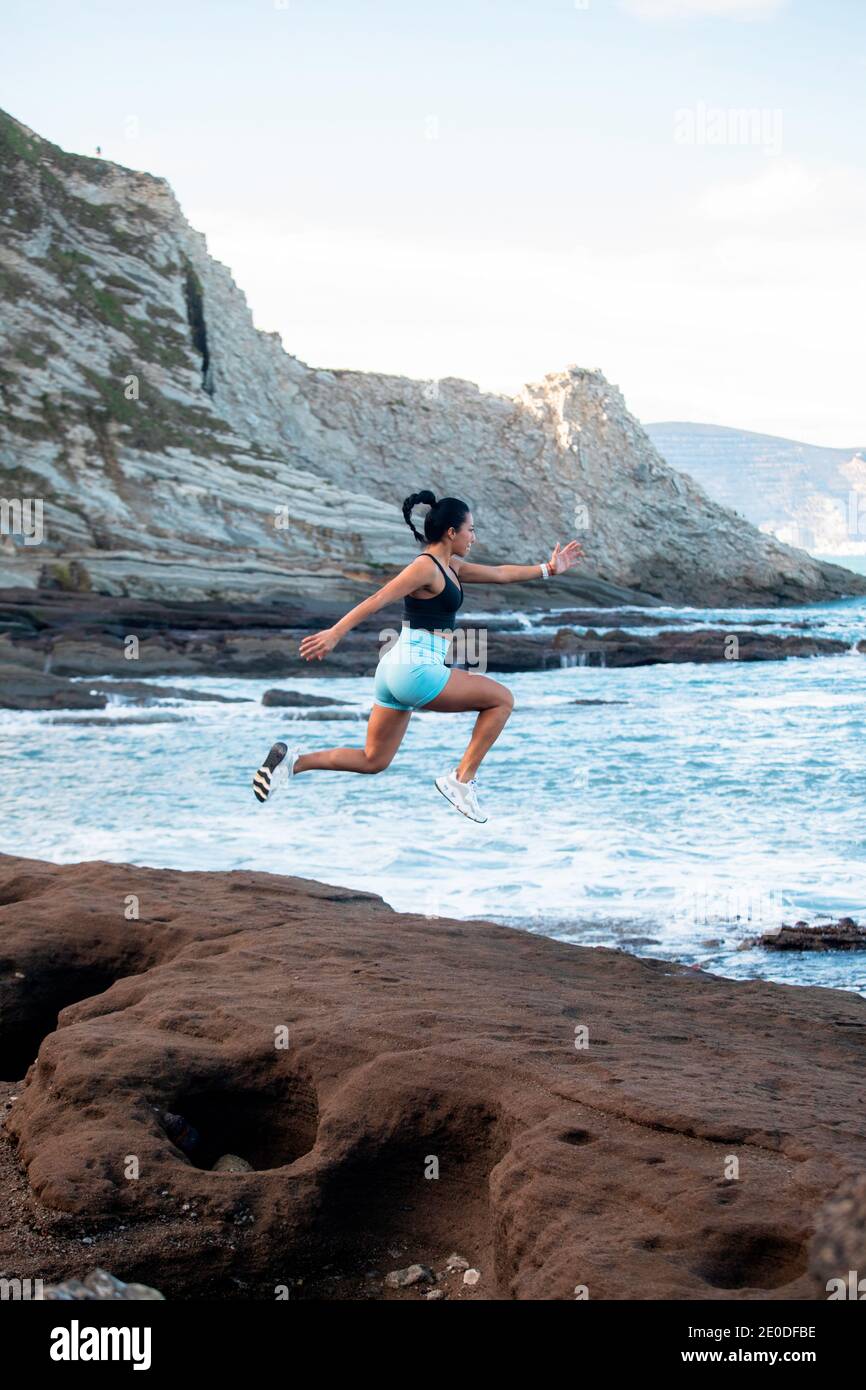 Side view of athletic female jumping high above ground while doing ...