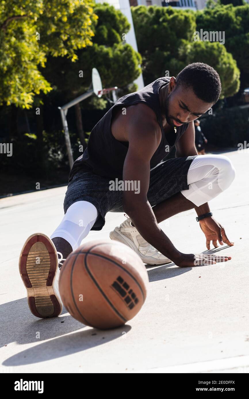 Fit African American male basketball player warming up legs and doing ...