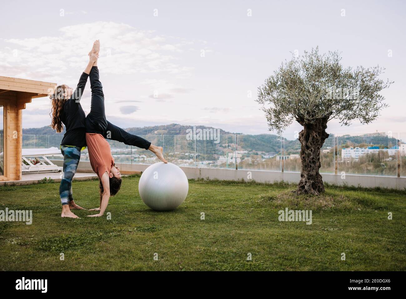 Side view of female personal yoga instructor helping man with handstand ...