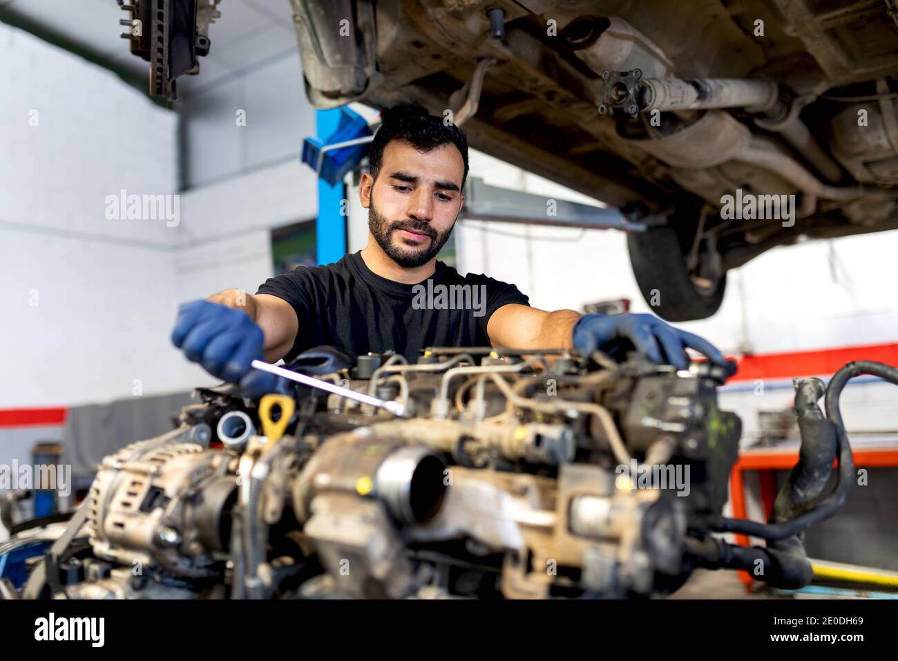 Busy bearded male mechanic with metal wrench repairing dirty car engine ...