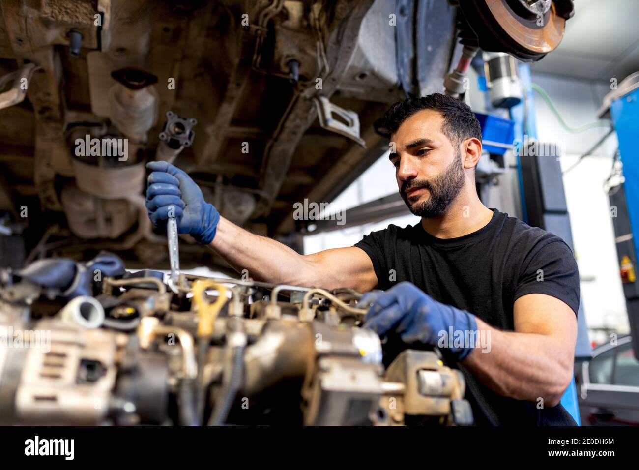 Busy bearded male mechanic with metal wrench repairing dirty car engine ...