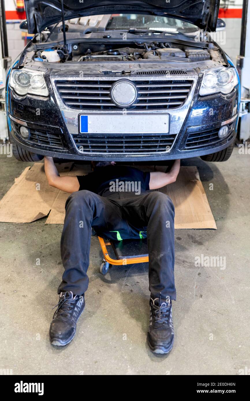 High angle of crop anonymous male mechanic lying on car creeper and ...