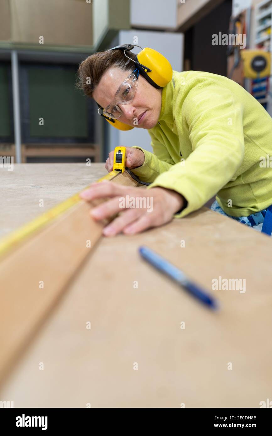 Low angle of concentrated middle aged female carpenter in uniform and ...