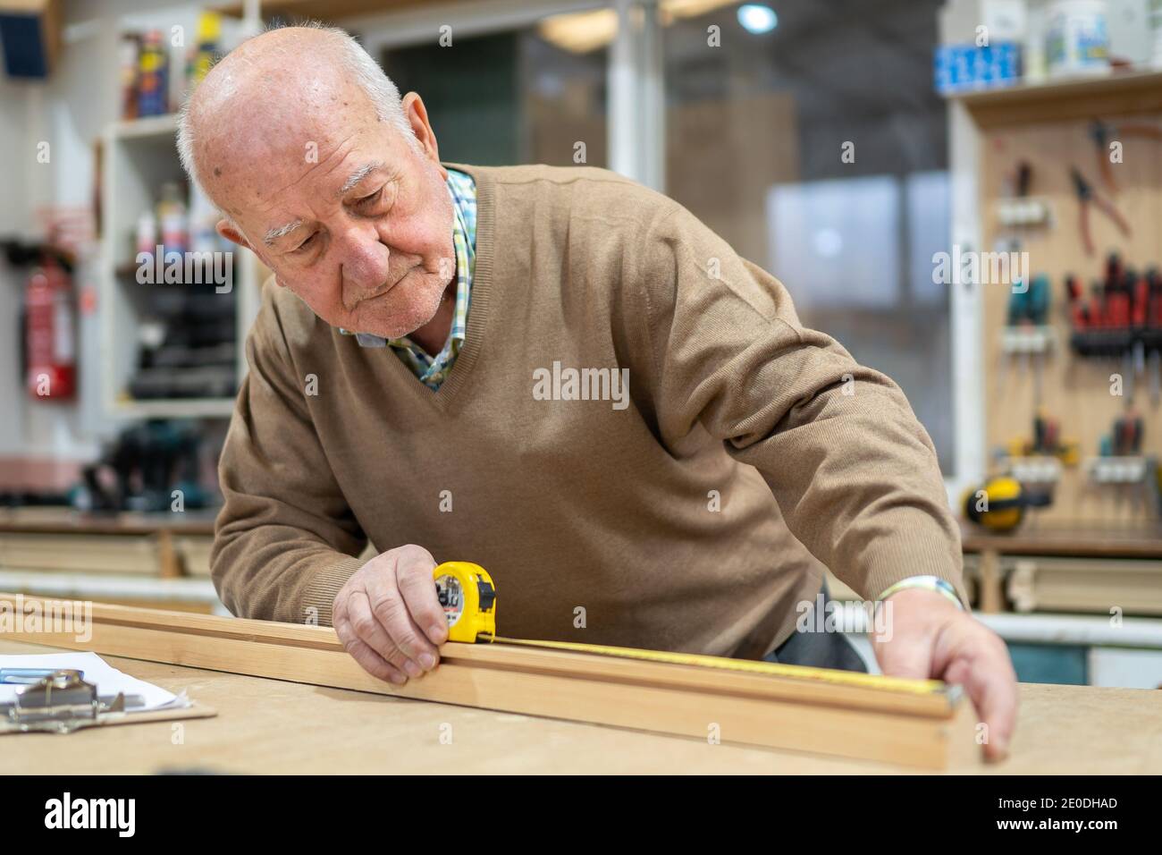 Elderly male woodworker measuring material with tape placed on machine ...