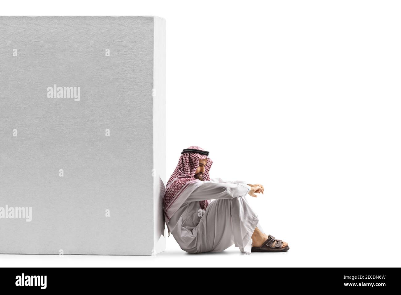 Sad saudi arab man sitting on the floor and leaning on a wall isolated ...