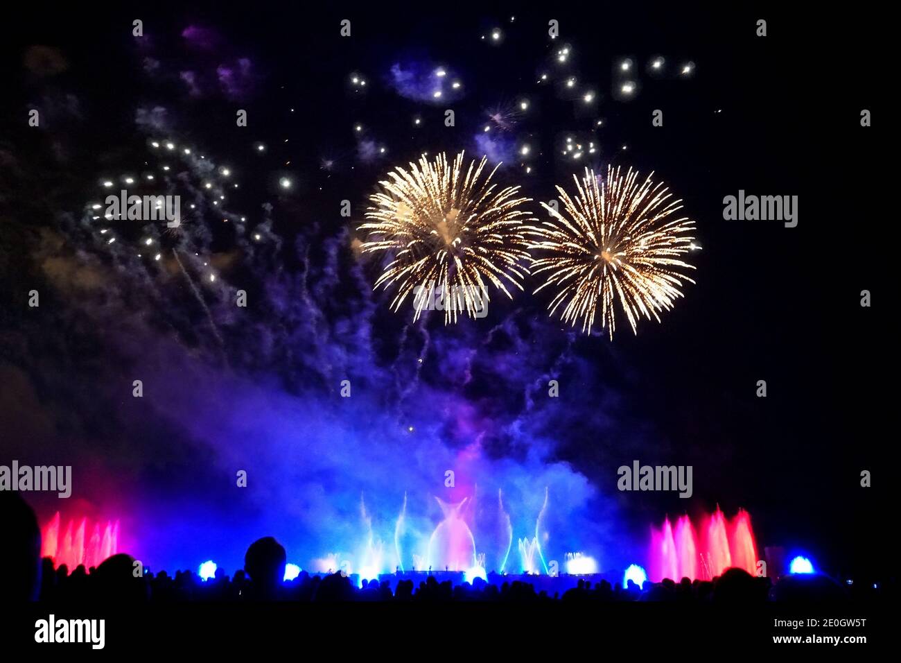 Beautiful fireworks on the dark sky above a lit water fountain with ...