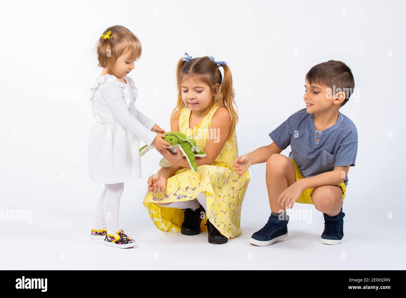 Two school kids and a toddler girl, playing with a cute big green ...