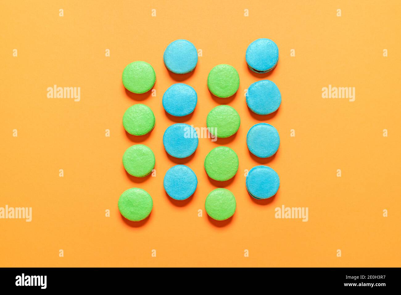 Blue and green macarons symmetrically aligned on an orange background ...