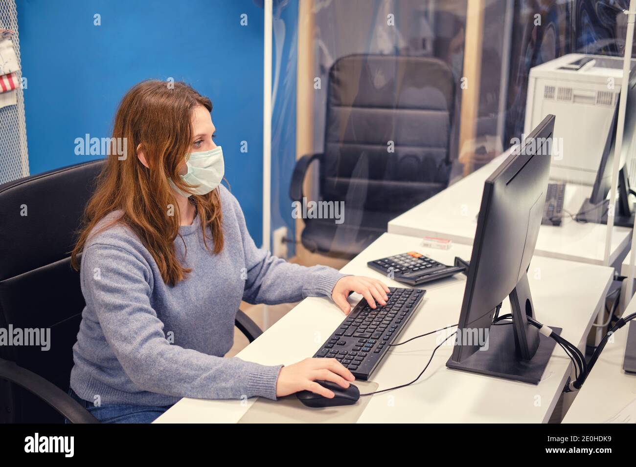 An office employee works on a computer in a room with glass partitions ...