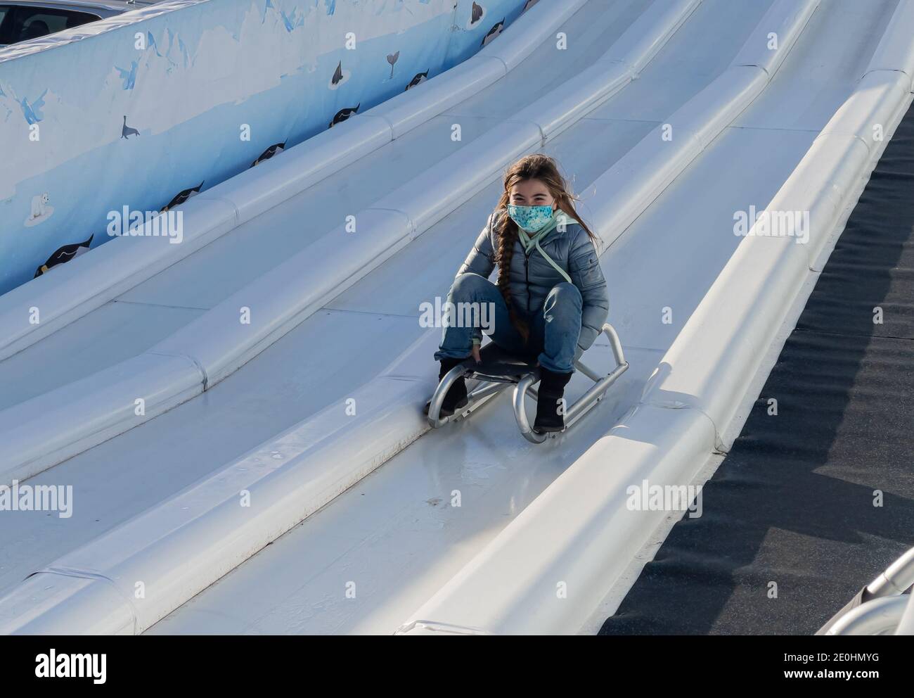 Child wearing medical mask while riding a sled at ice slide during ...