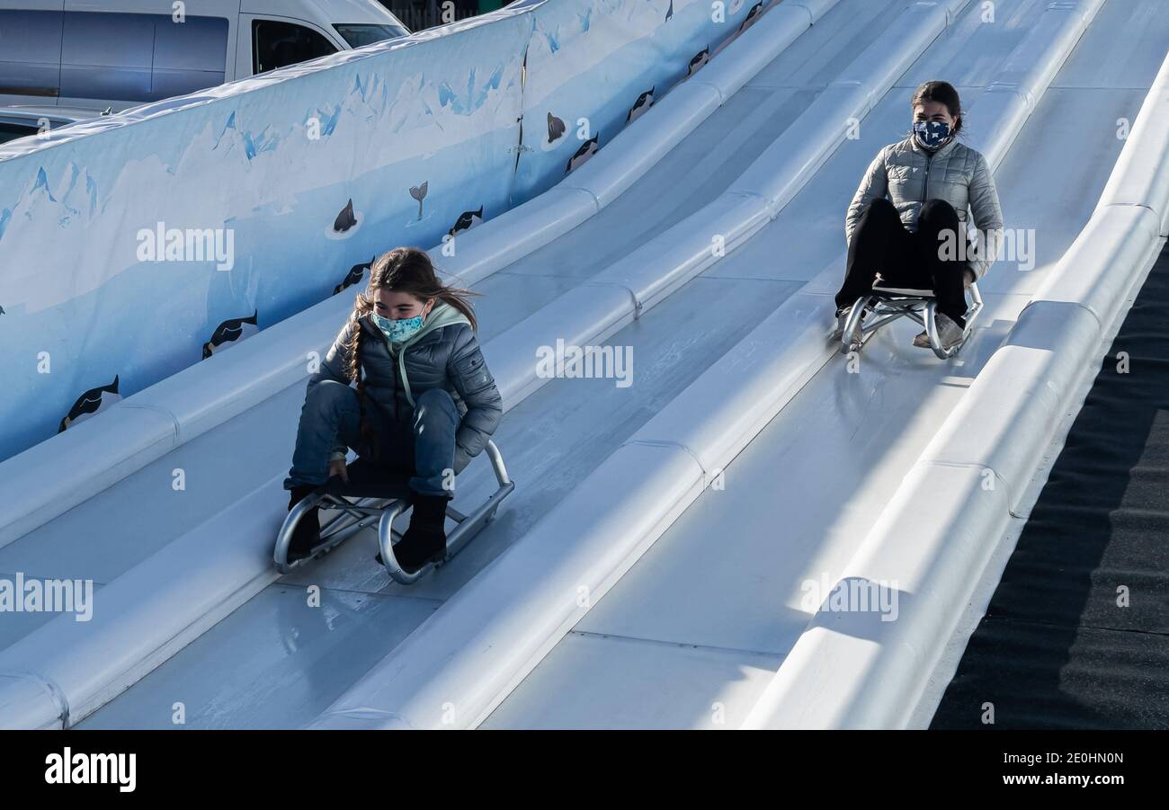Mother and daughter wearing medical mask while riding sleds at ice ...