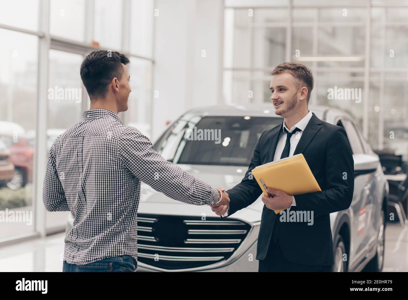 Professional car salesman smiling, shaking hands with his male customer ...