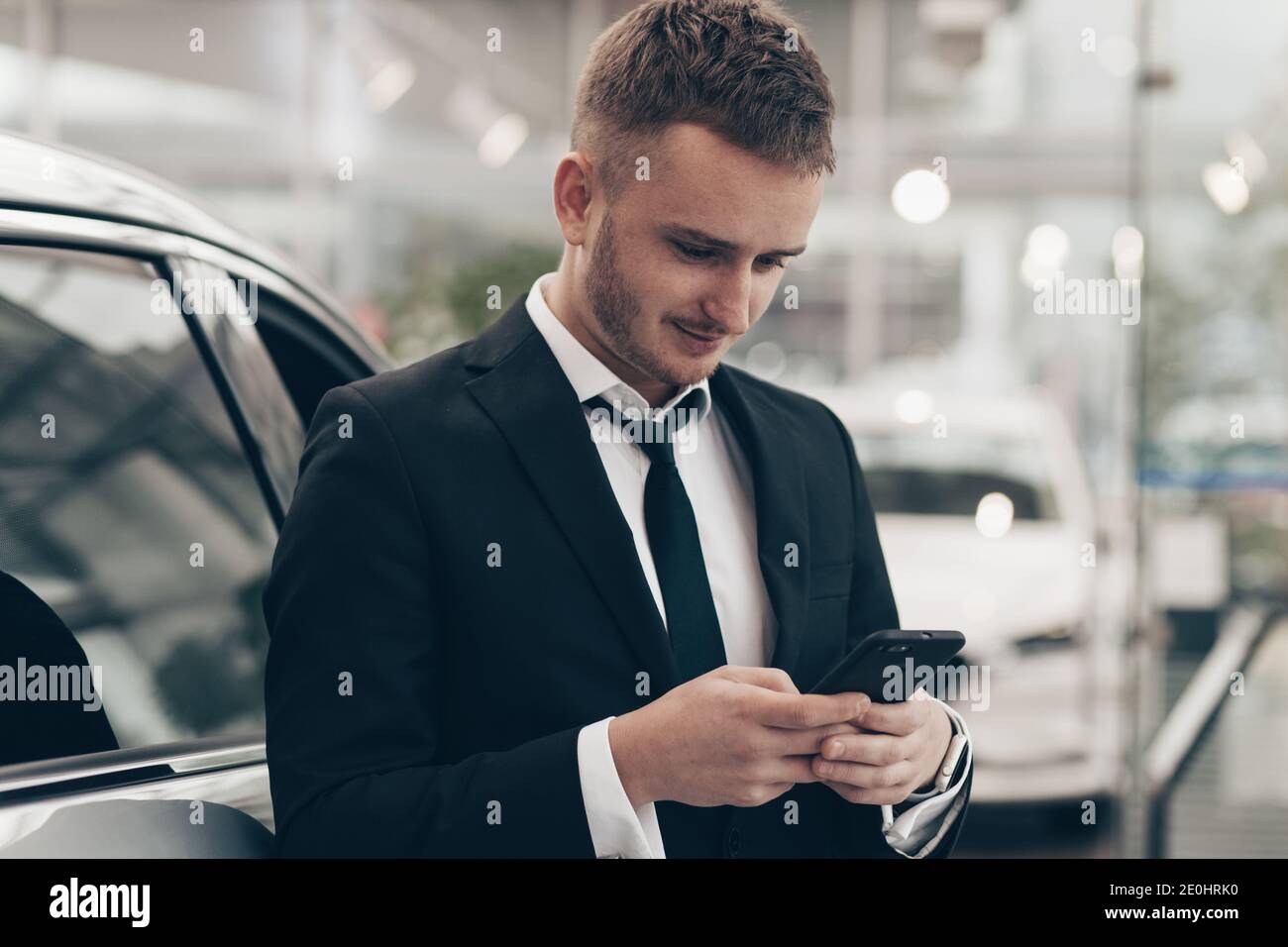 Businessman using his smart phone at the car dealership. Young salesman ...