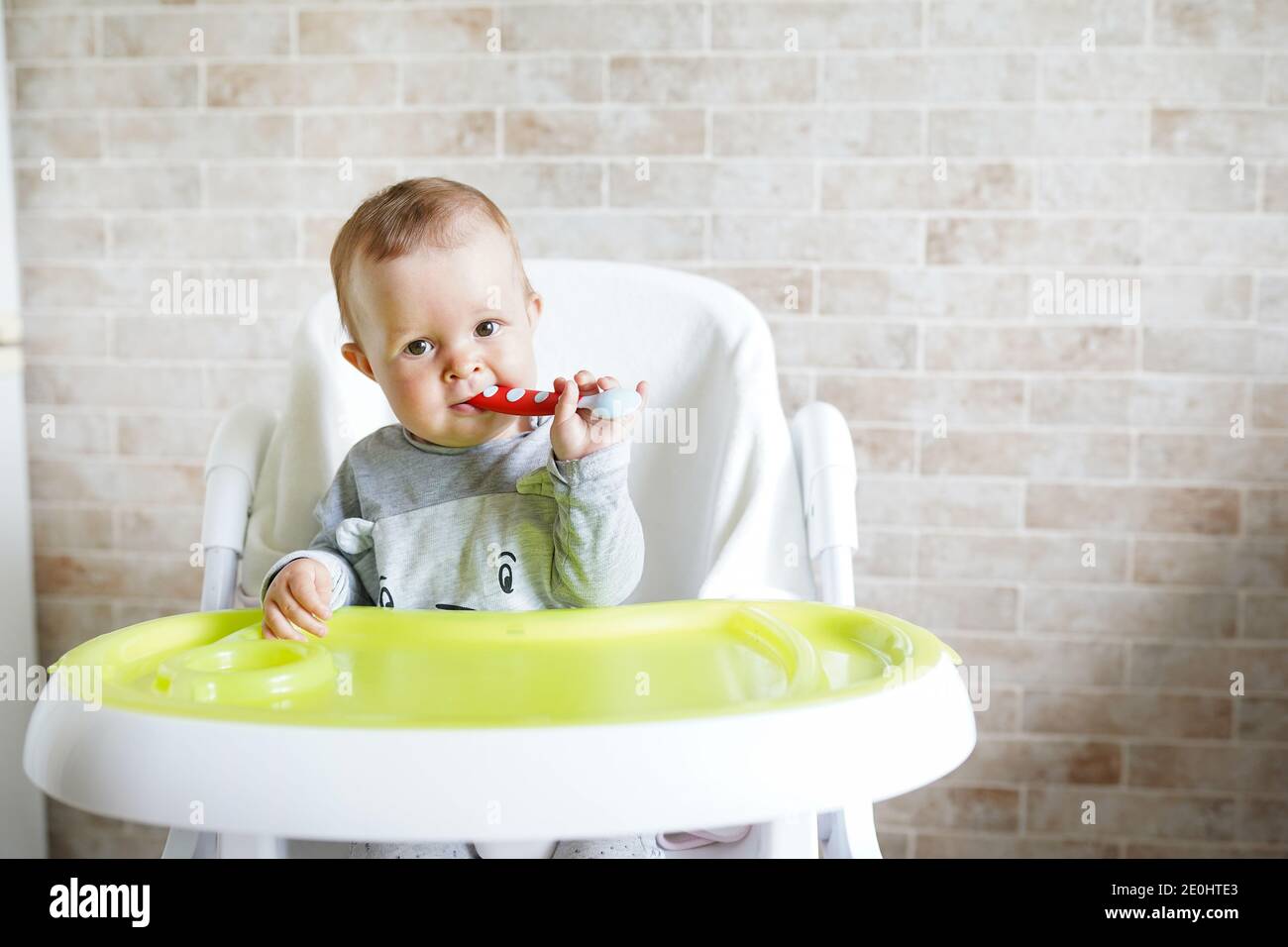baby child eating with spoon in sunny kitchen. Portrait of happy kid in ...
