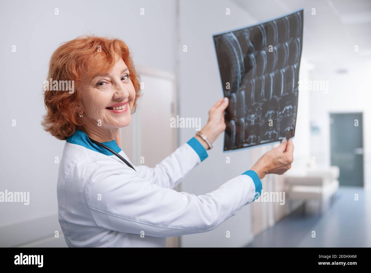 Friendly female oncologist smiling to the camera, holding MRI scan of a ...