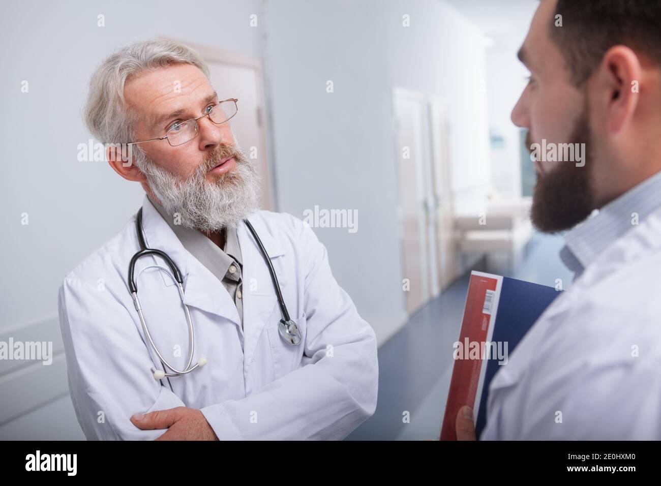 Elderly male doctor looking concerned, talking to his colleague at the ...