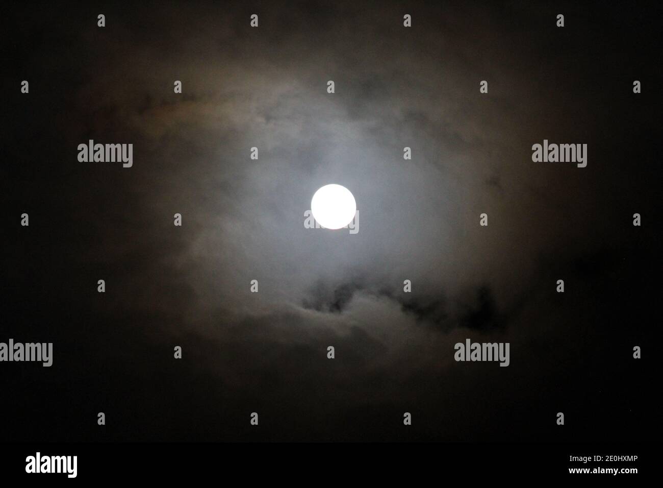 A dark night brings a bright, amber moon with puffy hazy clouds alive ...