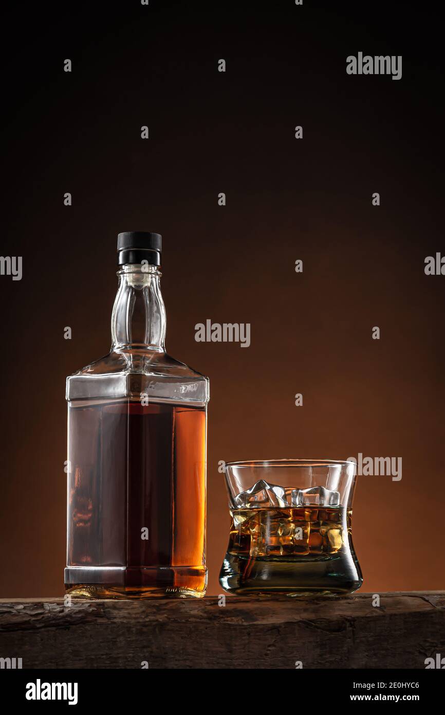 Bottle of whisky and glass of whisky with ice on wooden log with orange ...