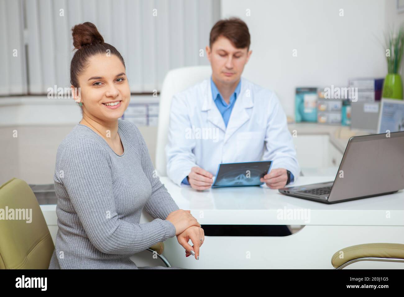 Happy healthy young woman smiling to the camera, her doctor examining x ...